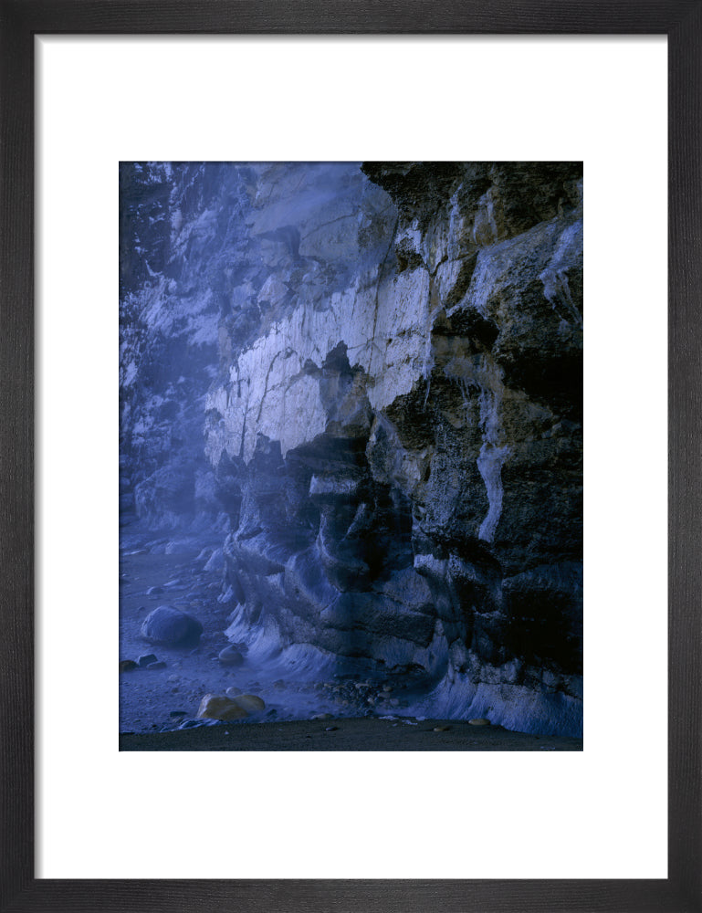 A half-frozen waterfall on the crumbling cliff face and on the rocky f ...