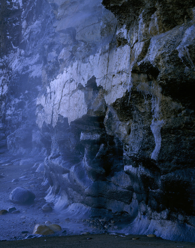 A half-frozen waterfall on the crumbling cliff face and on the rocky f ...