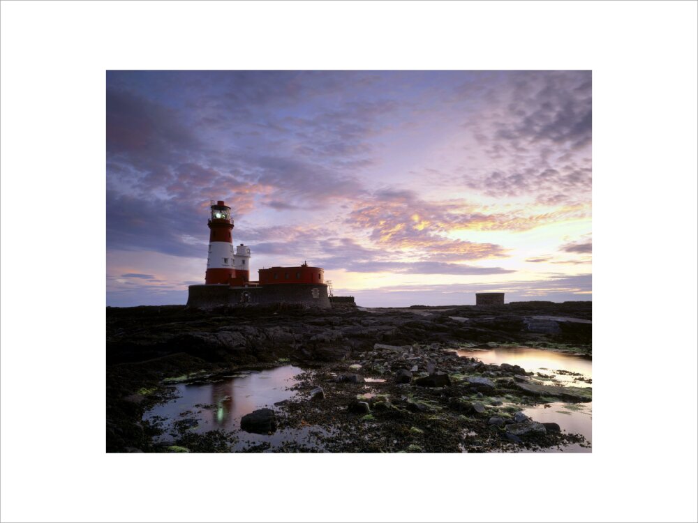 A view of Longstone Lighthouse across a rocky area with pools of water ...
